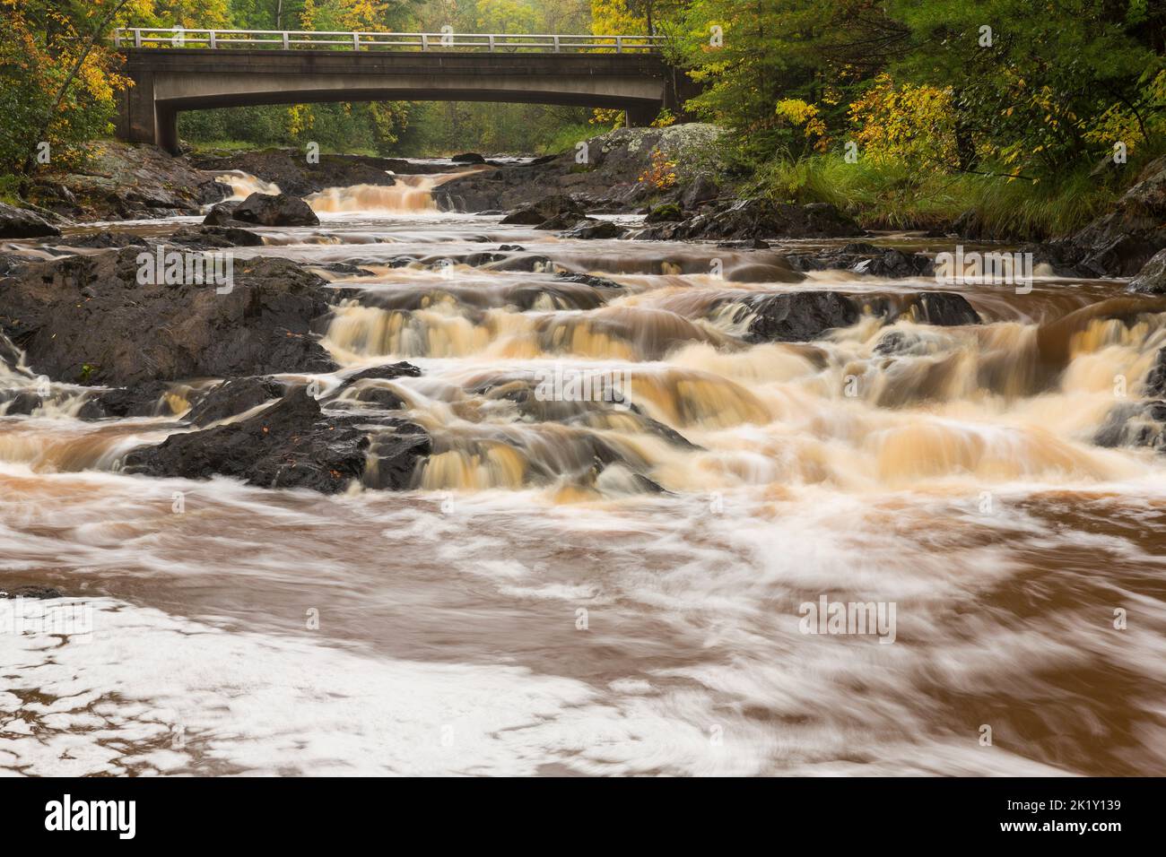 A cascading waterfall under a bridge in the woods during autumn Stock ...