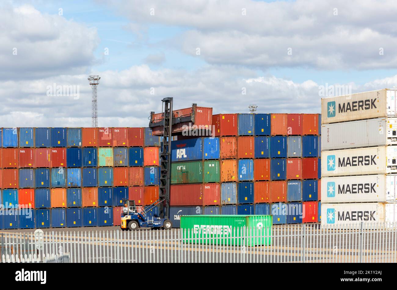 Containers stacked in piles lifted by toplifter machinery on quayside ...