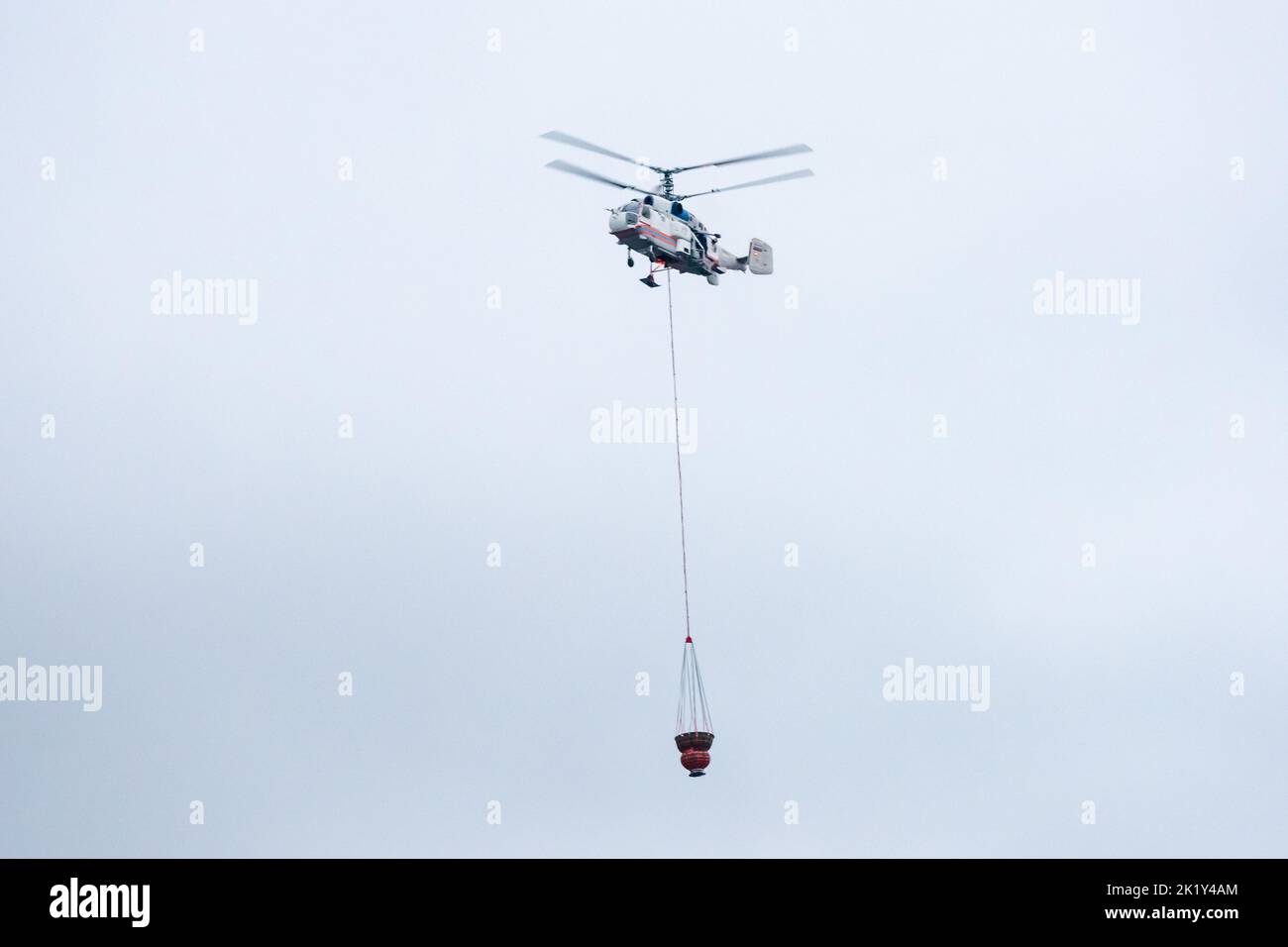 A fire helicopter carries a container of water to extinguish a fire in ...