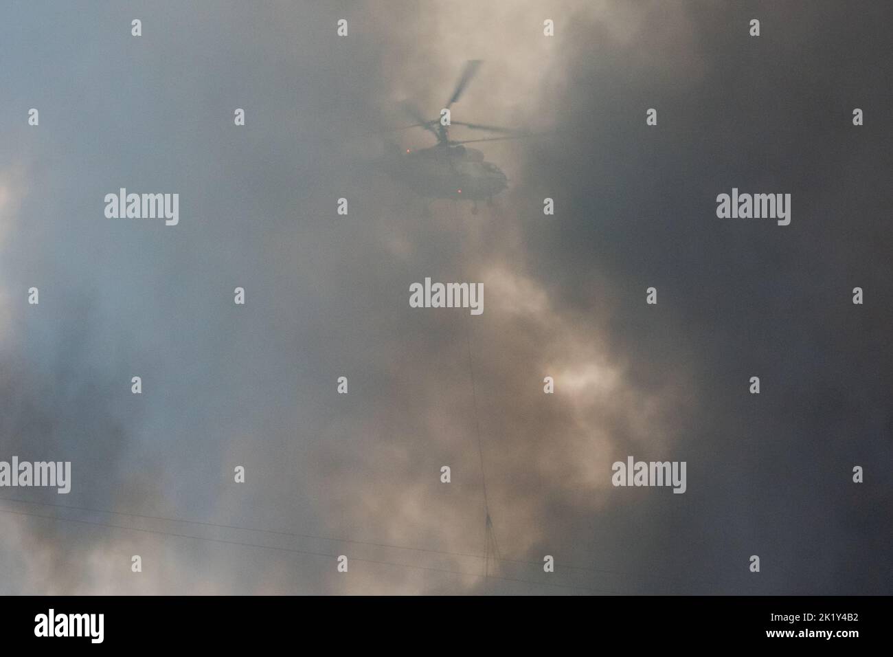 A fire helicopter carries a container of water to extinguish a fire in ...