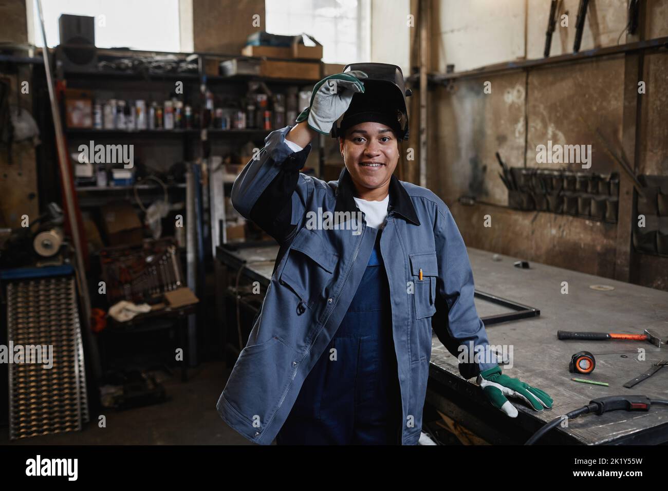 Waist up portrait of multiethnic female welder smiling at camera in ...