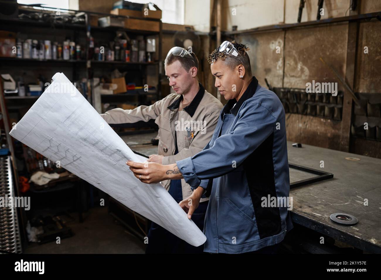 Side view portrait of two workers looking at blueprints in industrial ...