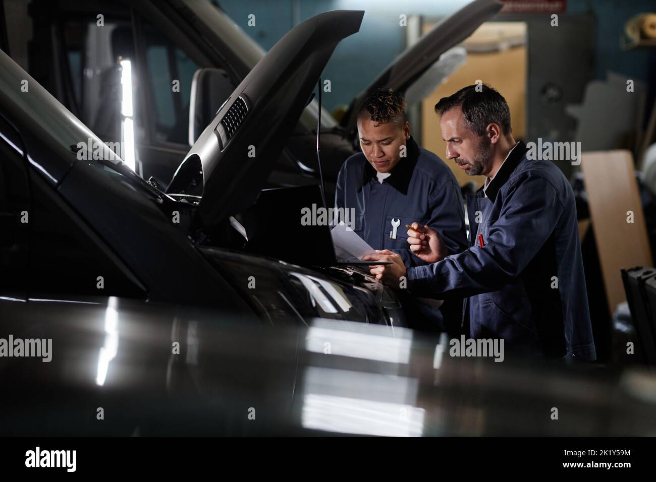 Side view portrait of two mechanics using laptop during car checkup in ...