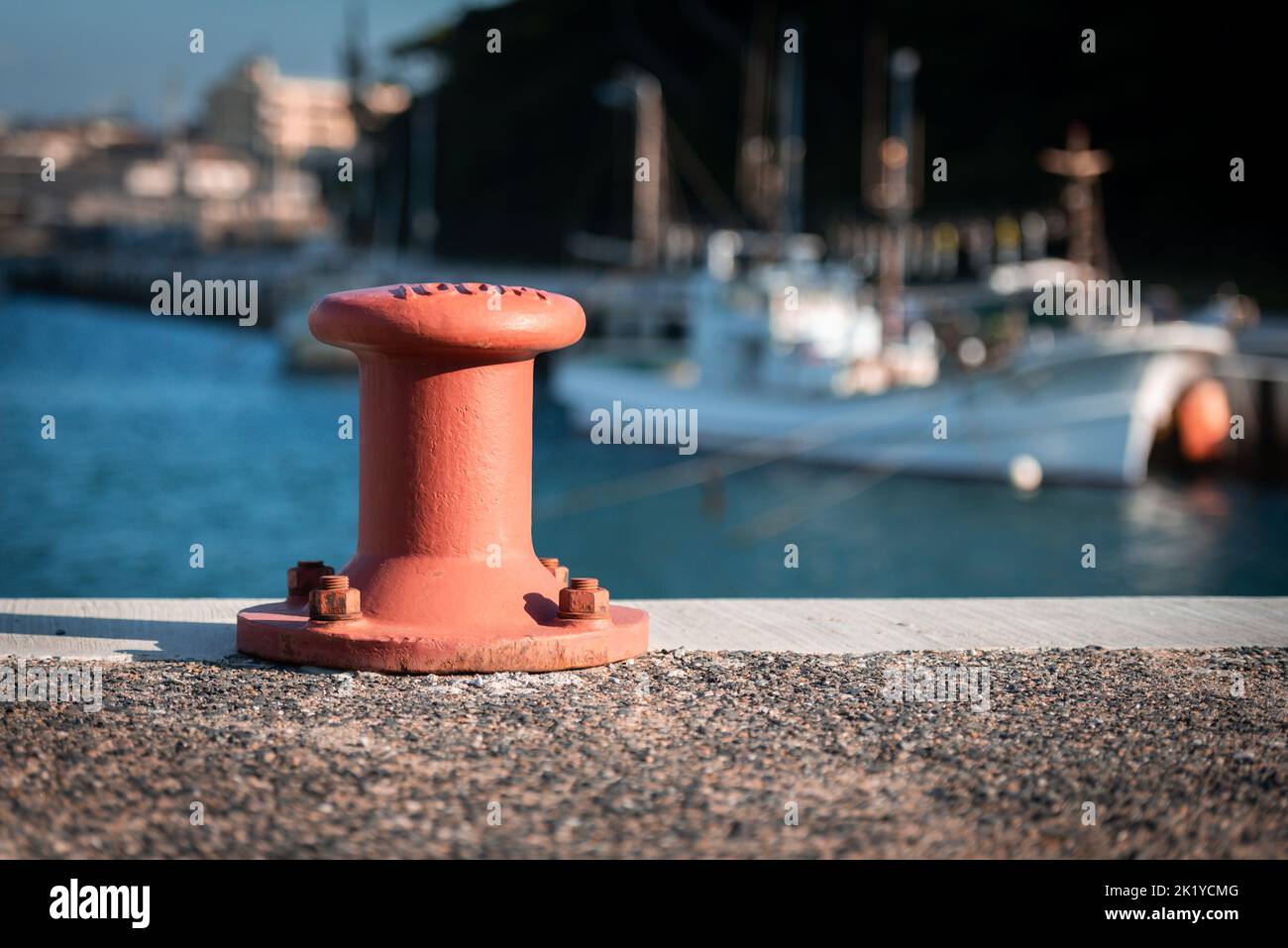 A red orange mooring bollard with a fishing boat in the background ...