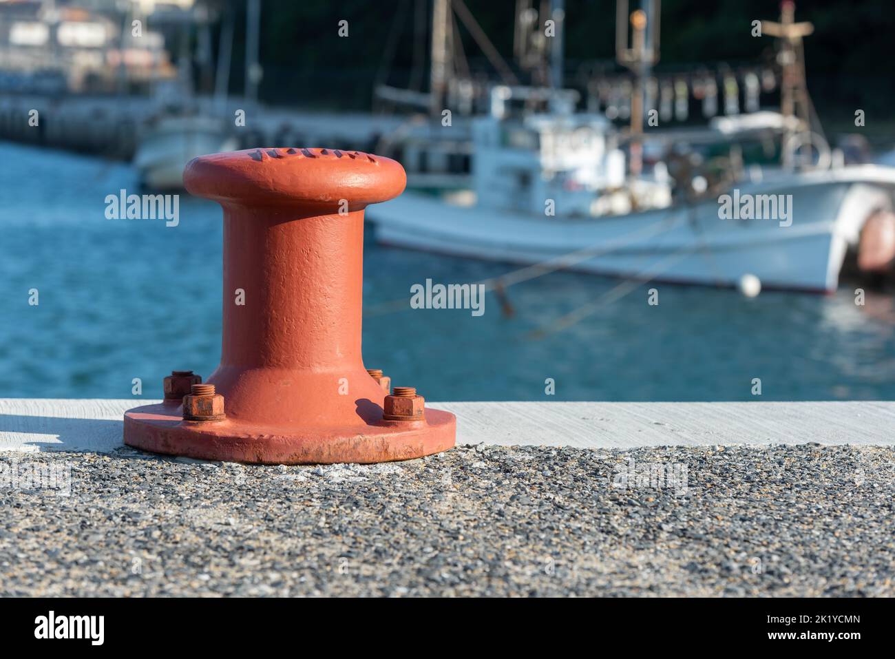 A red orange mooring bollard with a fishing boat in the background ...