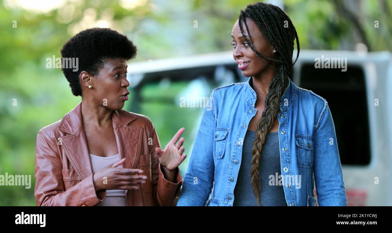 Two female friends in conversation walking outside in street talking ...