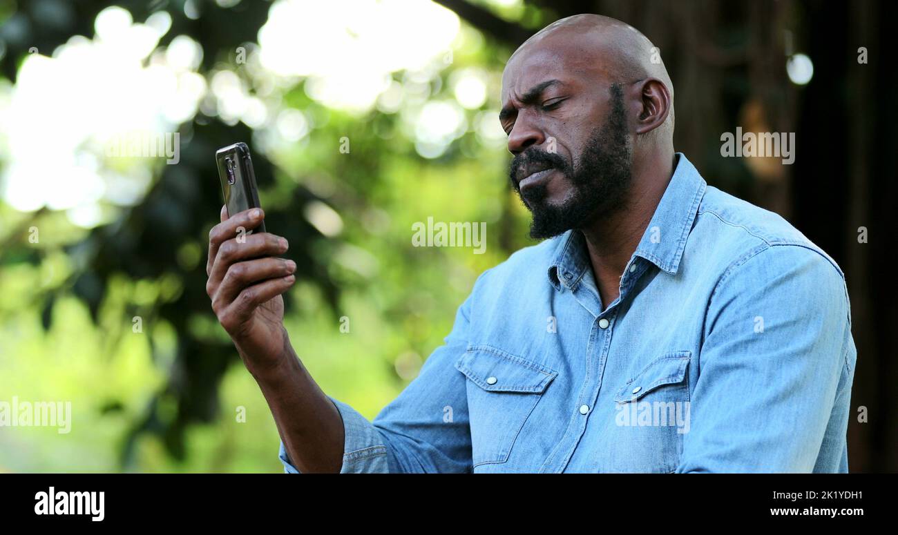 Sad African man holding smartphone in despair receiving bad news Stock ...