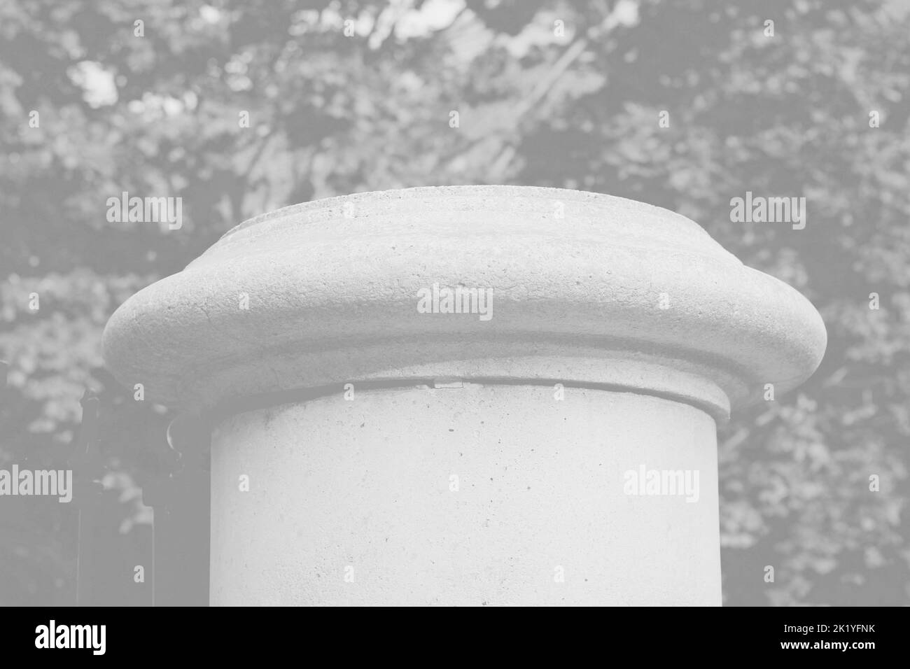 The top of a round column standing in the garden in a faded black and ...