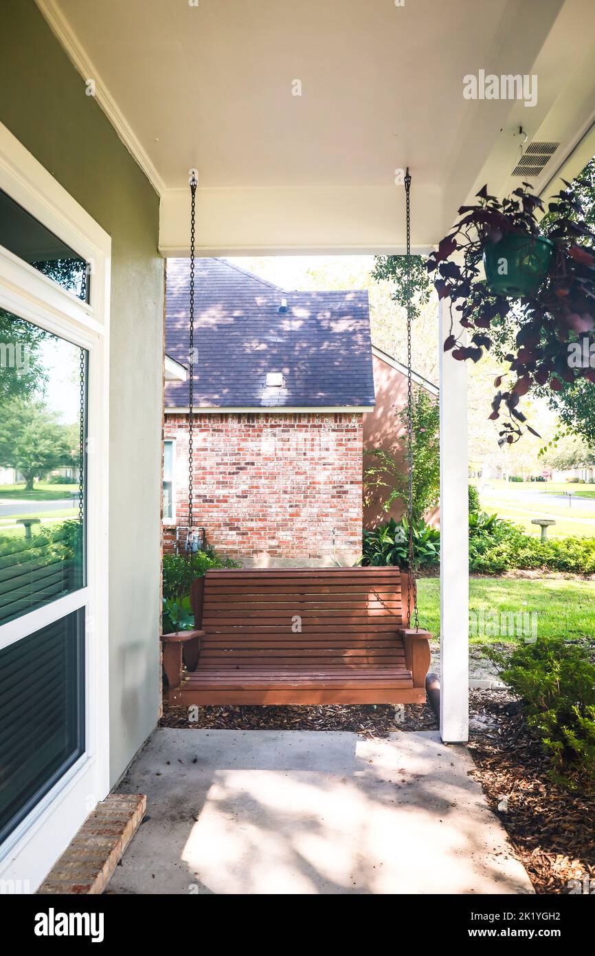 A wooden brown outdoor porch swing on a small front porch of a house ...