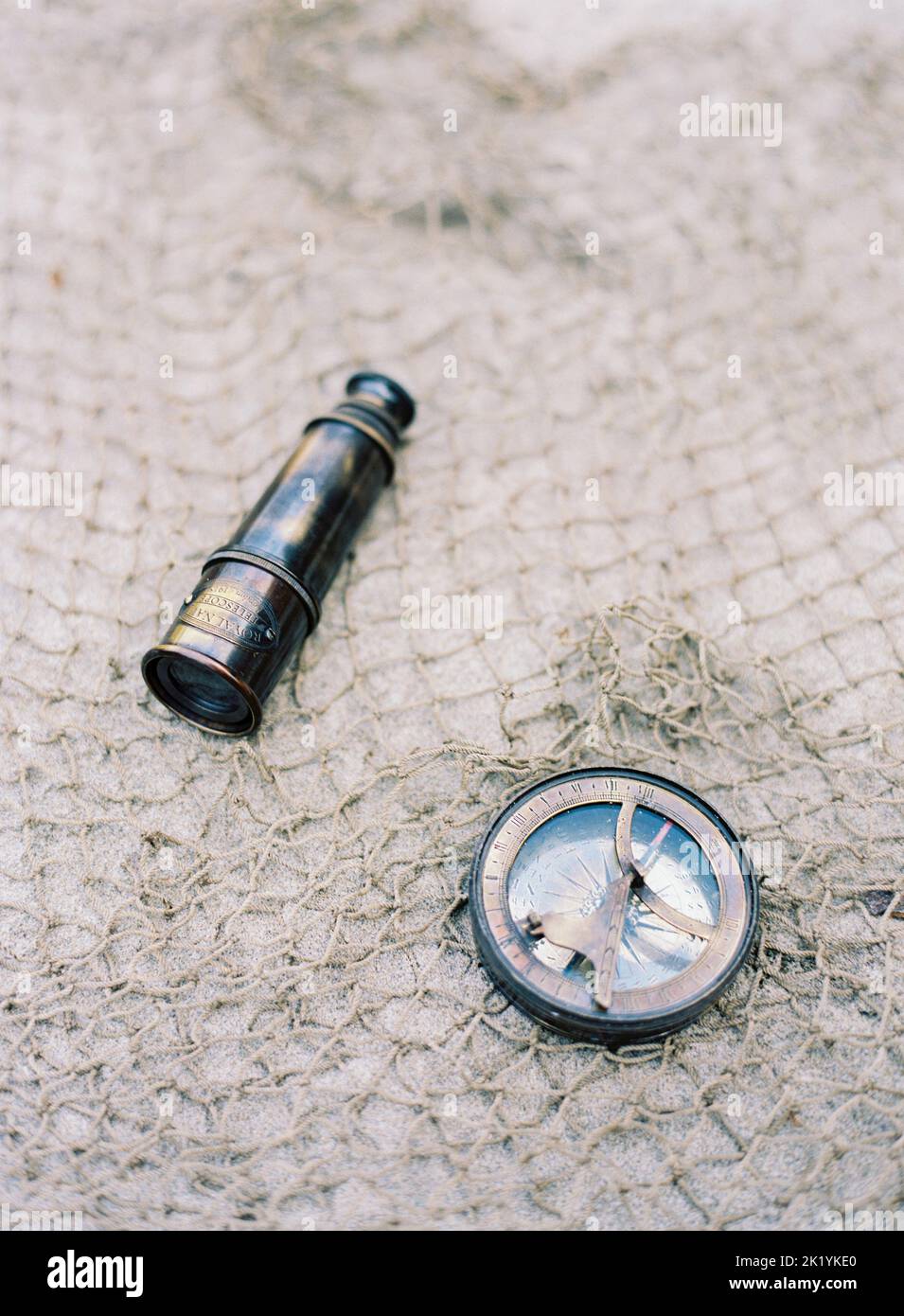 An antique nautical telescope and old metal compass on texture mesh net ...