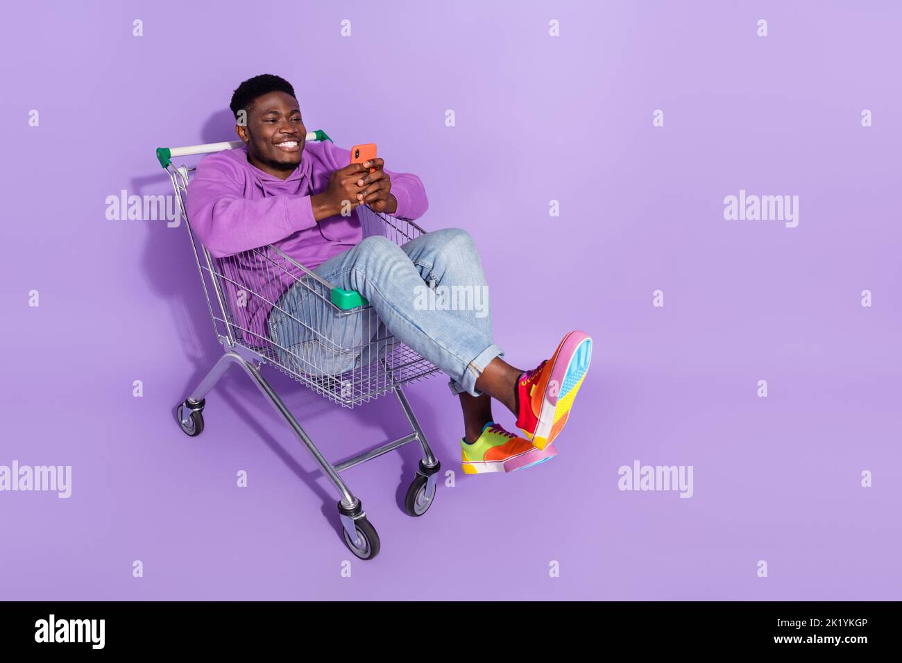 Full body portrait of funny positive guy sitting trolley use telephone ...
