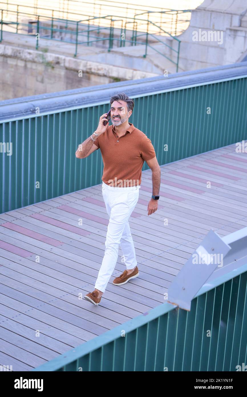 Stylish middle-aged man talking on the phone while walking outdoors ...