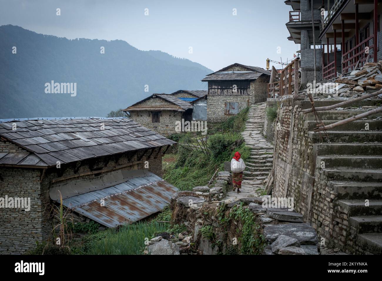 A lady walks carrying a big bag on her back through the Himalayan town ...