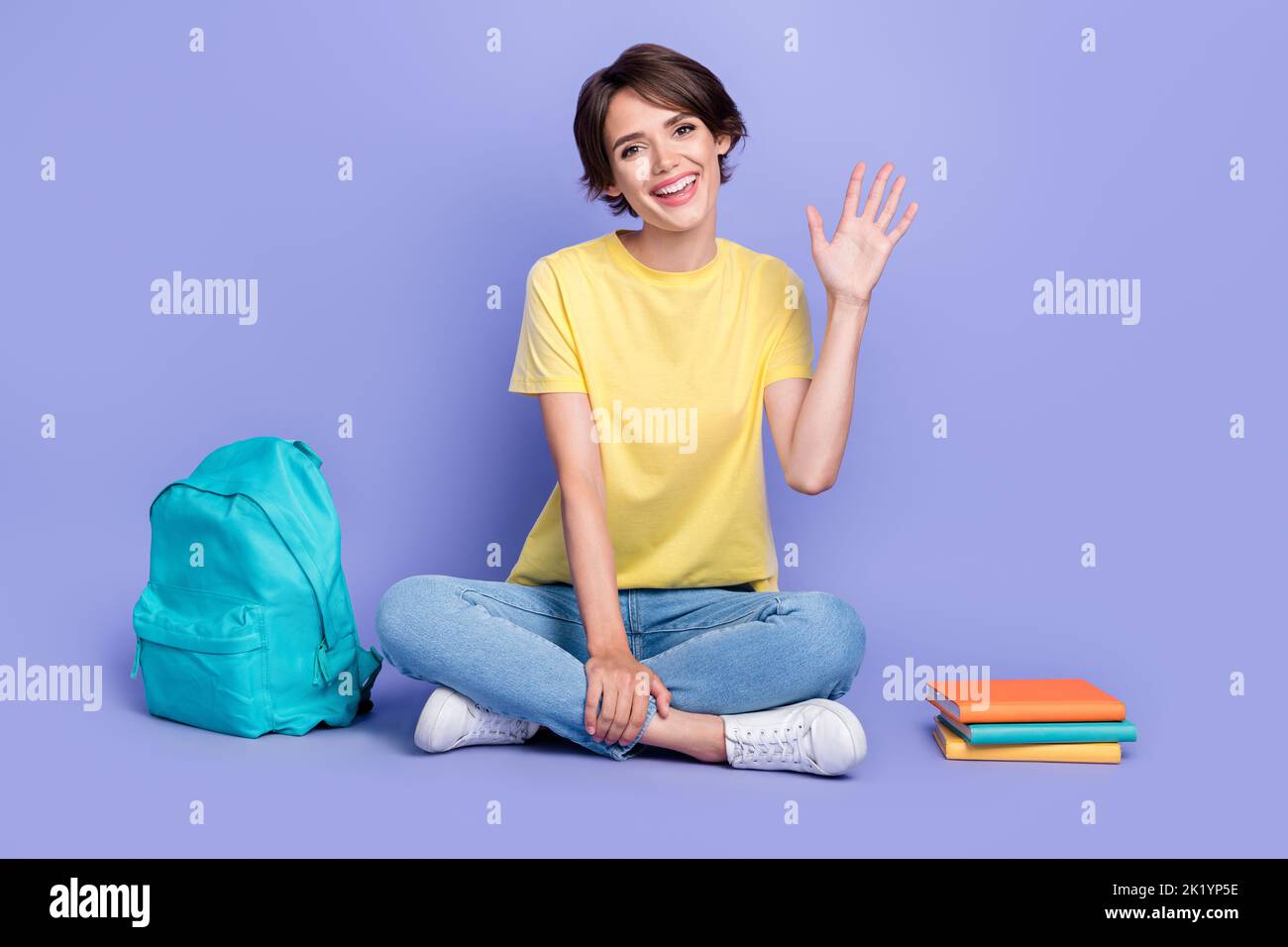 Full length photo of charming positive person sit floor arm palm waving ...