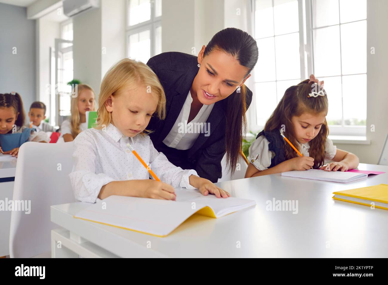 Friendly young female teacher helping little students with test tasks ...