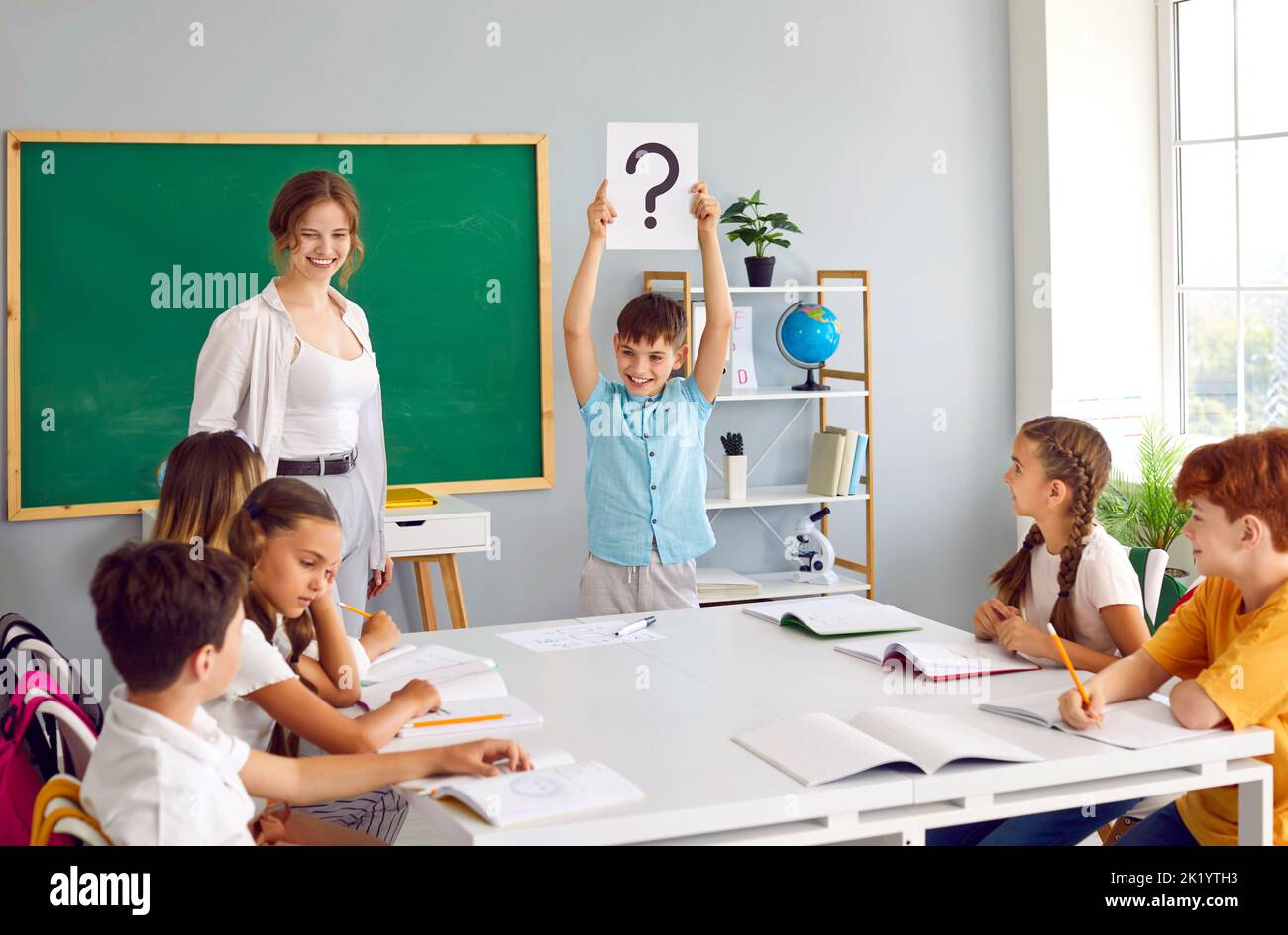 Cheerful schoolchildren solve logical problems together with teacher in ...