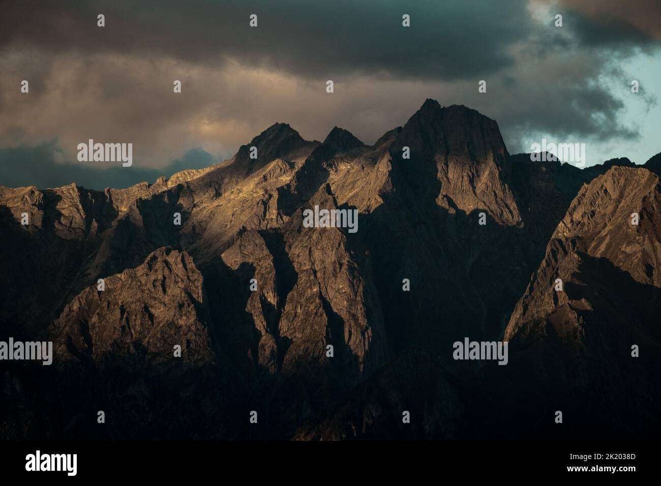 A dark mountain with sun rays hitting the peak and clouds at the ...