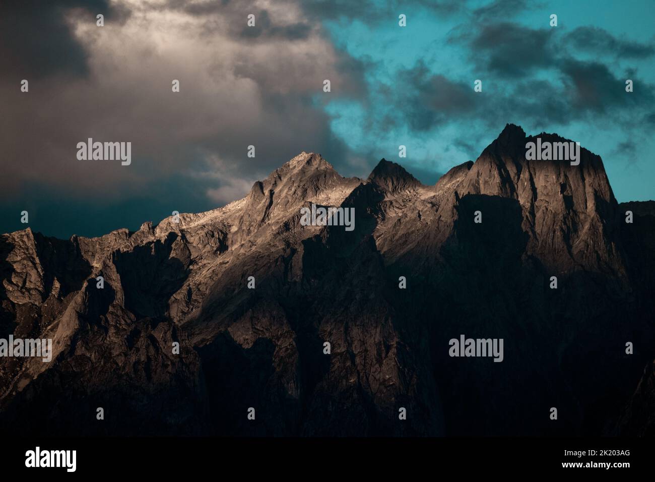 A dark mountain with sun rays hitting the peak on a semi-cloudy day ...