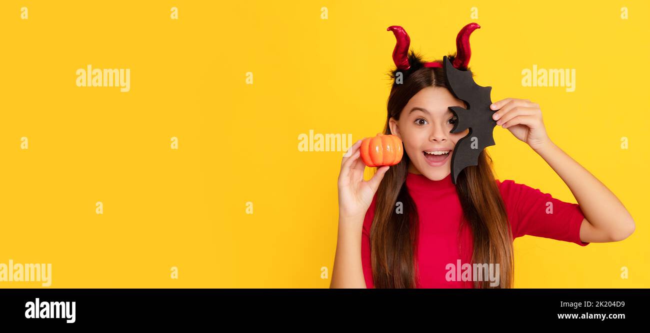 amazed child in imp horns hold pumpkin and bat on yellow background ...