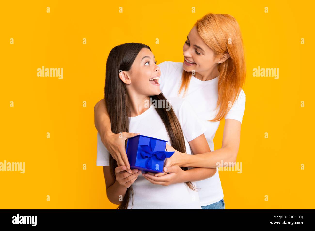 Mother and daughter with present gift. Teenager girl giving gift box to her mother on yellow ...