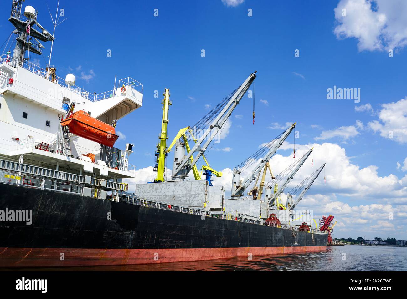 Large bulk carrier with open holds in harbor cargo terminal, shore ...
