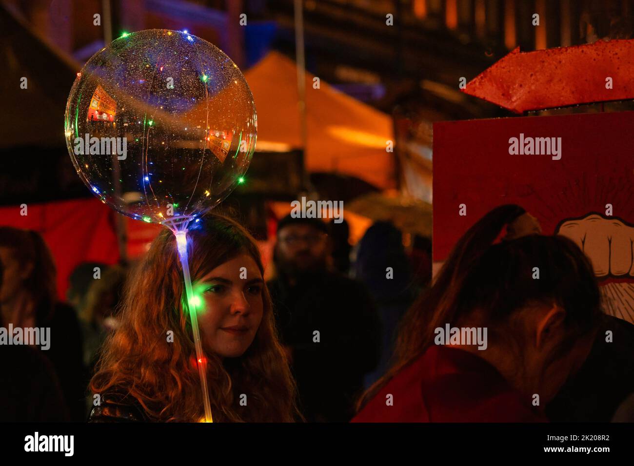 A transparent helium balloon is held on a long LED pole by a teenage ...
