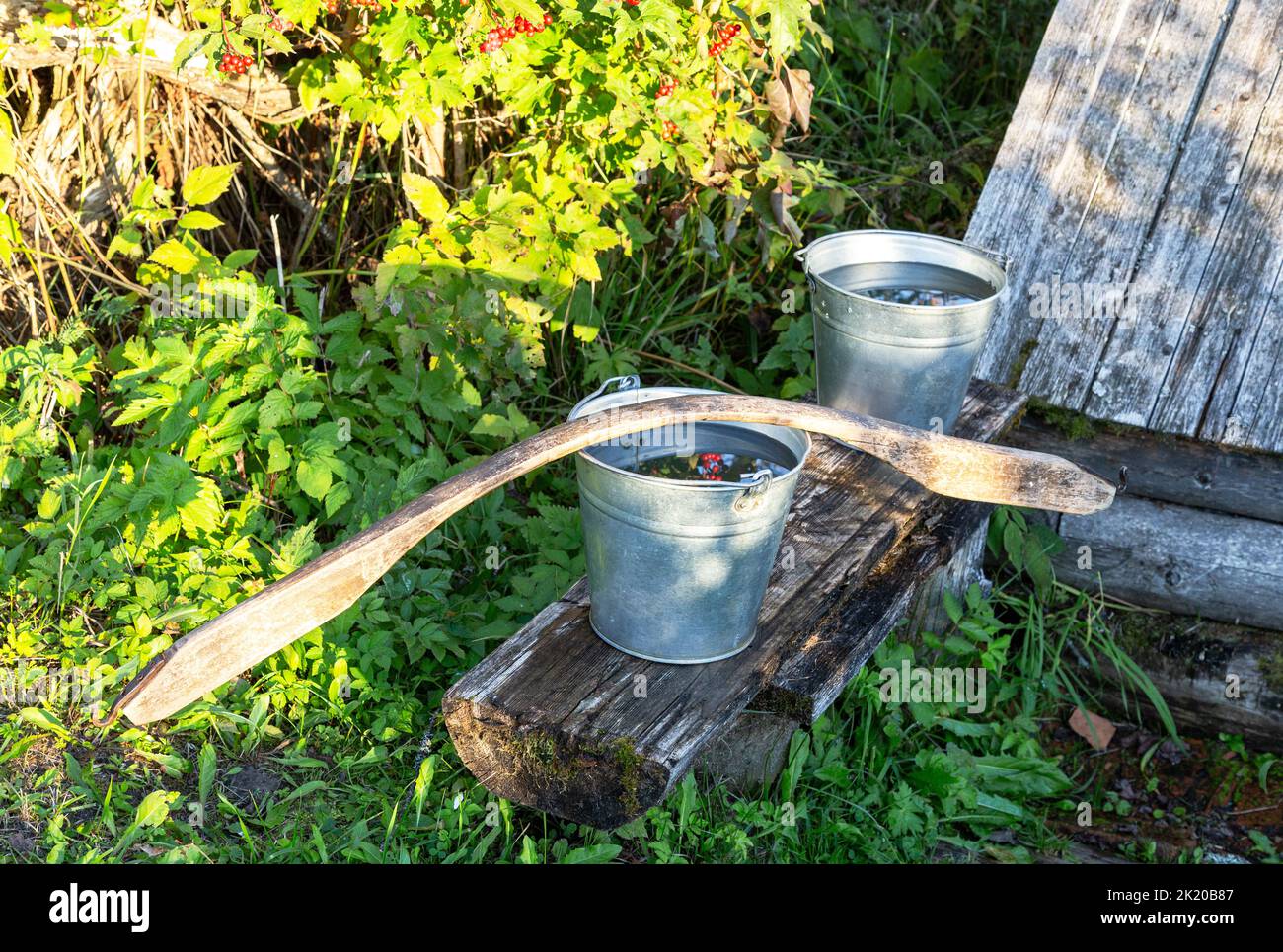 Metal buckets with water and shoulder yoke on a bench near a village ...