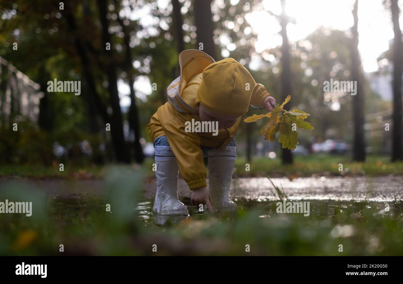 girl in yellow jacket and white rubber boots is running over a puddle ...