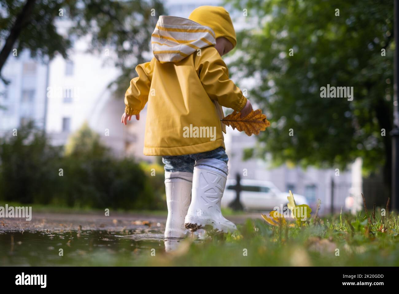 girl in yellow jacket and white rubber boots is running over a puddle ...