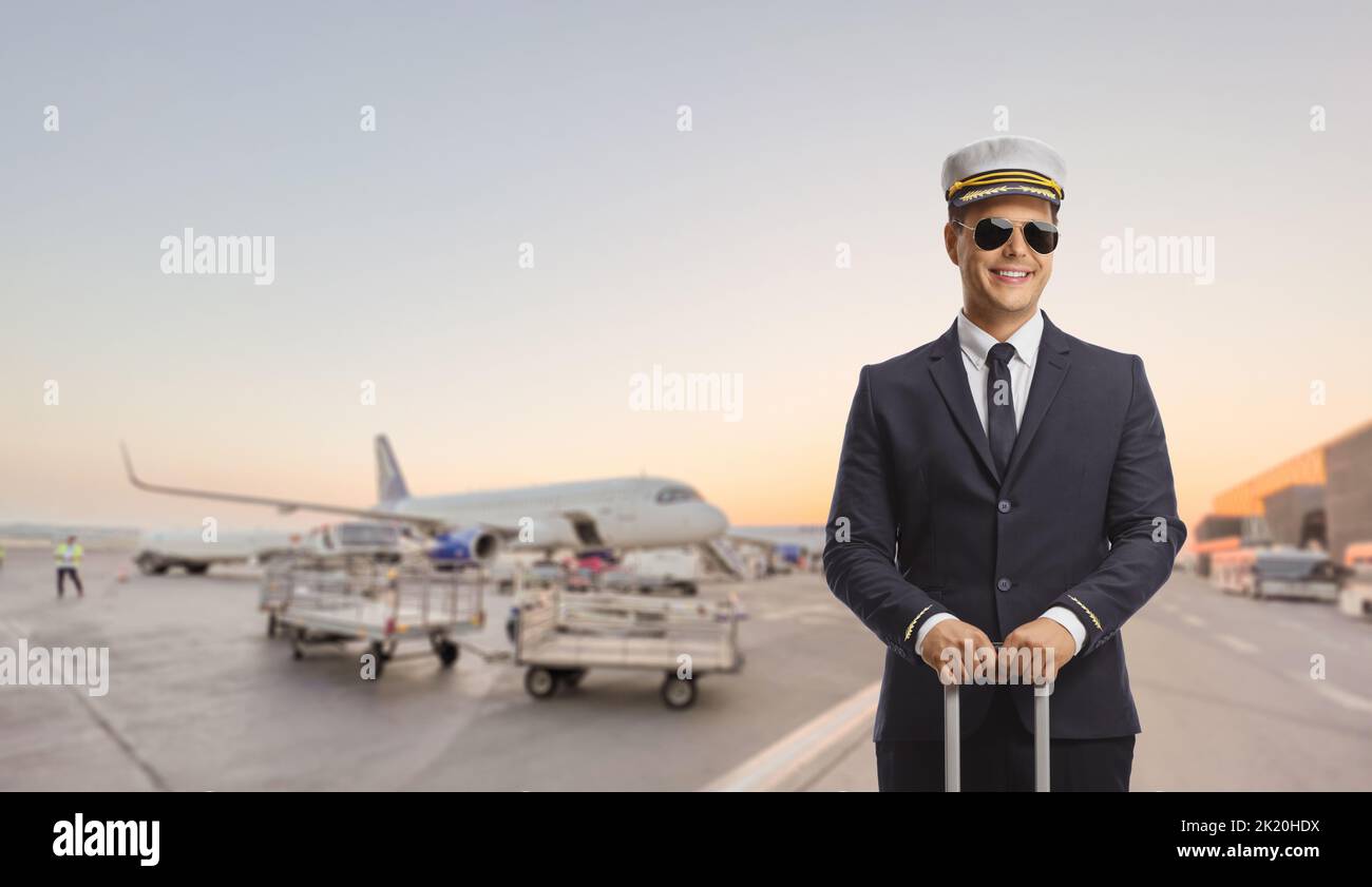 Young pilot standing with a suitcase on an airport with plane in the ...