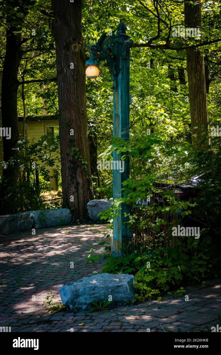 Green wooden lamp post with lit bulb among trees in a paved alley Stock ...