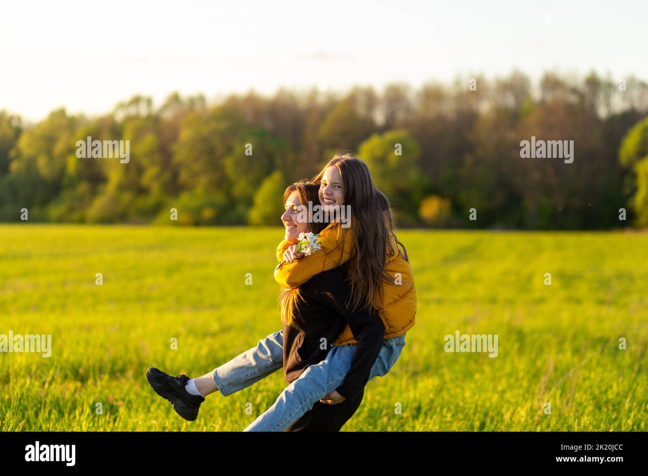 Playful mother giving daughter piggy back ride at green field. Both ...