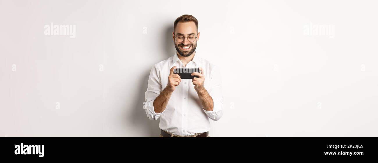 Happy businessman watching video on mobile phone, standing over white ...