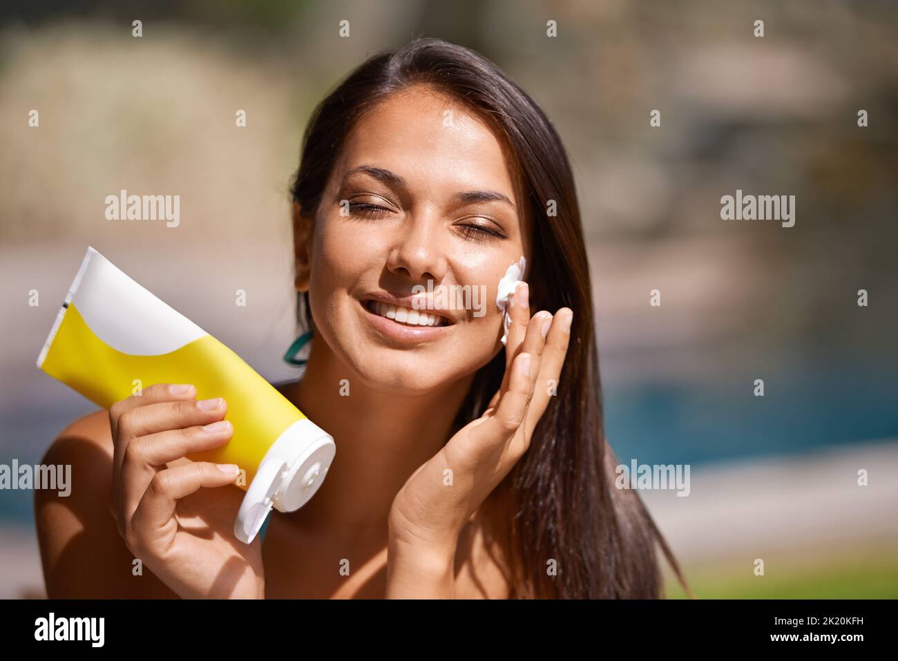 Protecting her beautiful skin. A beautiful young woman applying suntan ...