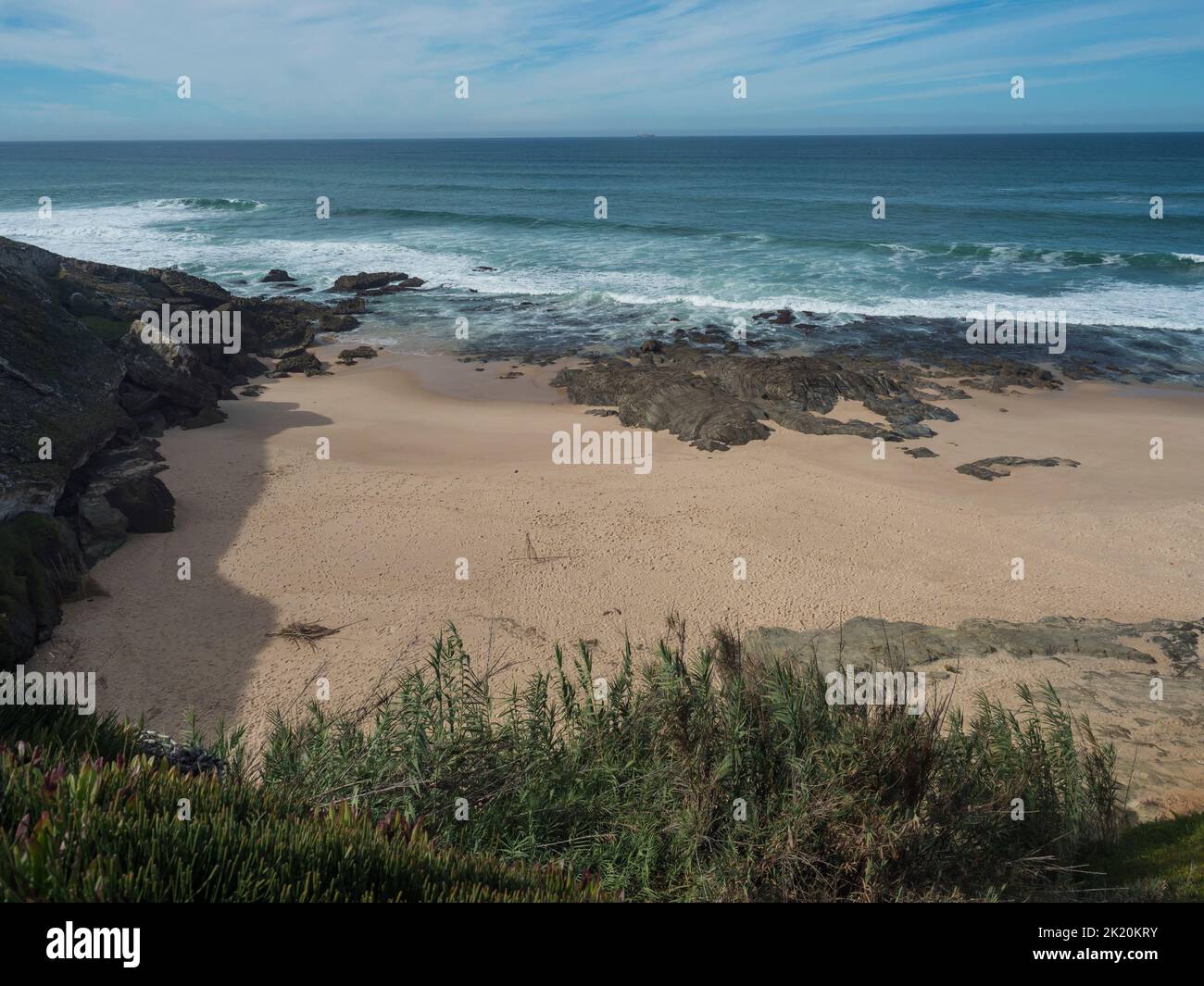 View of empty small sand beach with ocean waves and sharp rock and ...