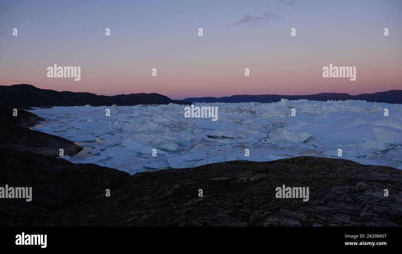 View from cliff overlooking bay of icebergs in Greenland at night Stock ...