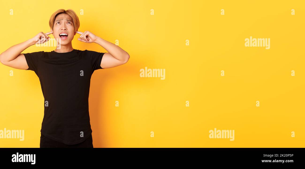 Portrait of annoyed and bothered asian guy grimacing, shut ears ...