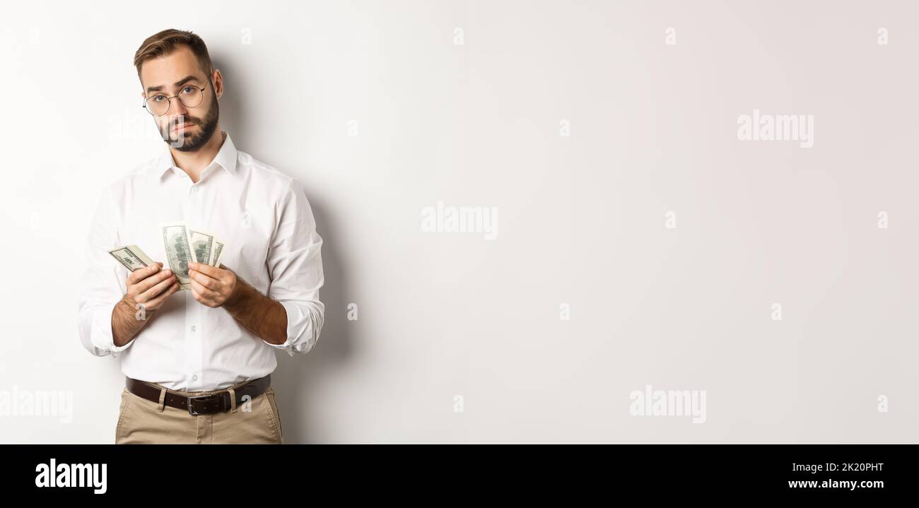 Handsome businessman counting money and looking at camera, standing ...