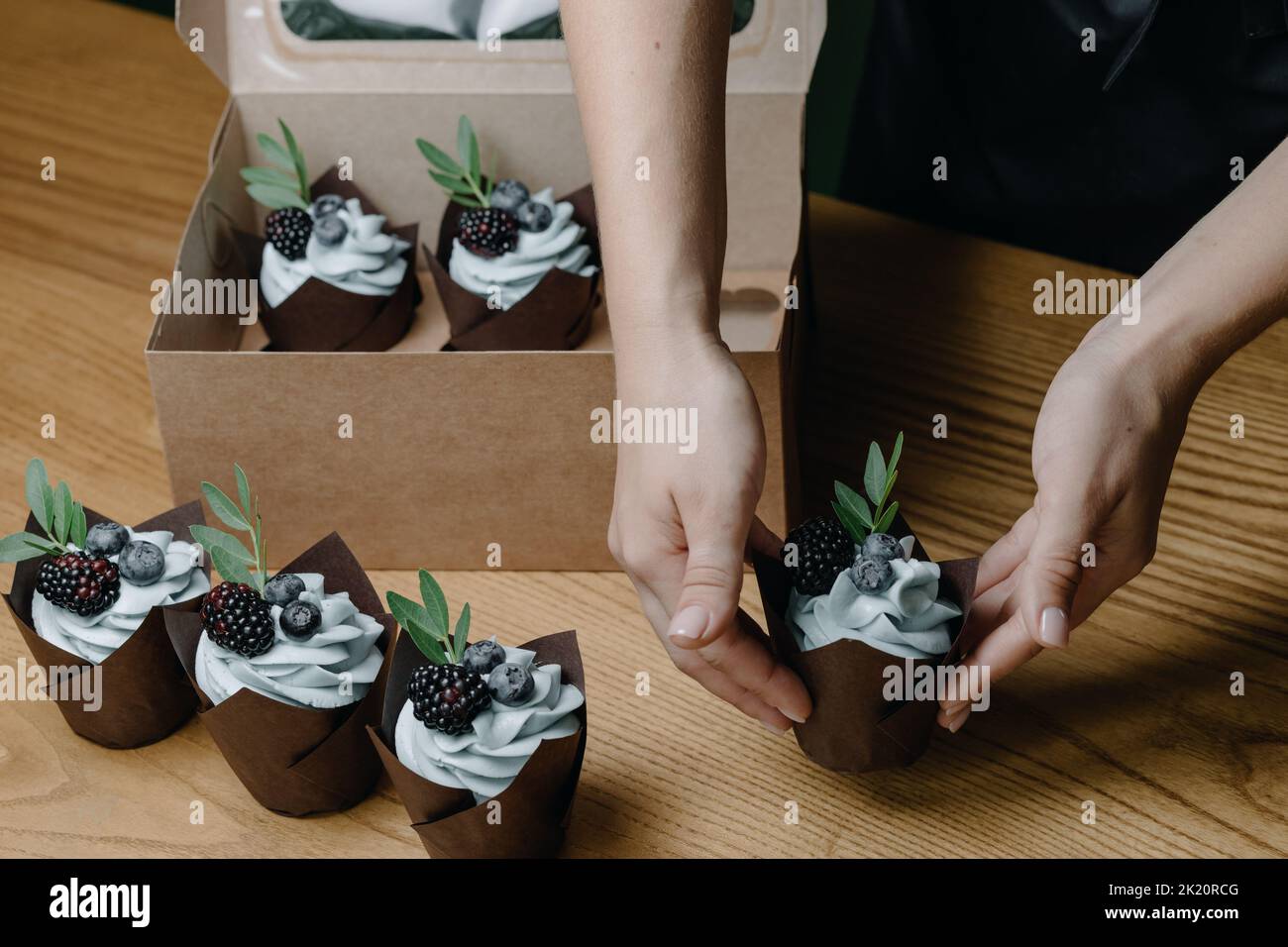 Close-up of female hands placing cupcake on table. Packaging of ...