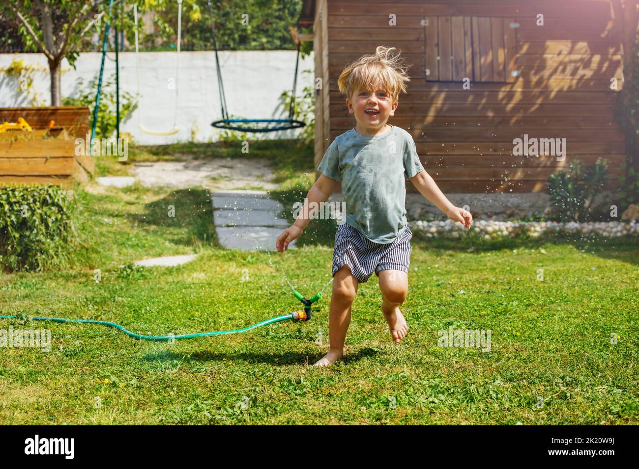 Fun in the garden - handsome boy run around water sprinkler Stock Photo ...
