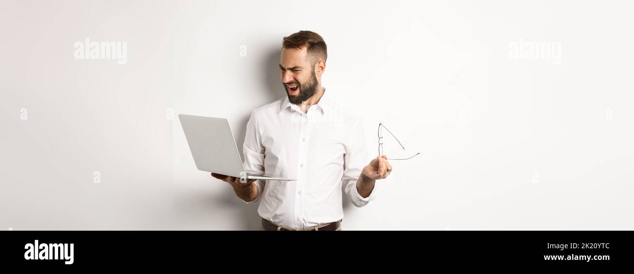 Confused manager looking at laptop, standing disappointed against white ...