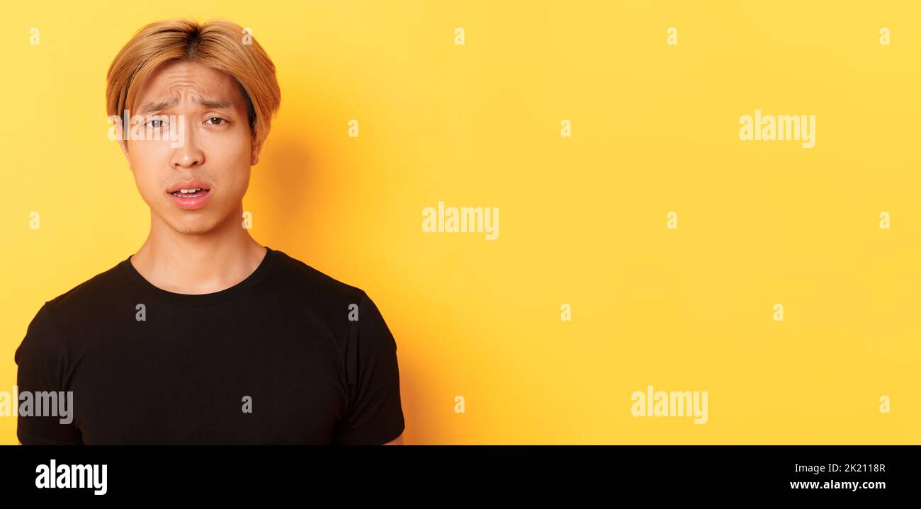 Close-up of confused and upset asian blond guy looking puzzled, open ...