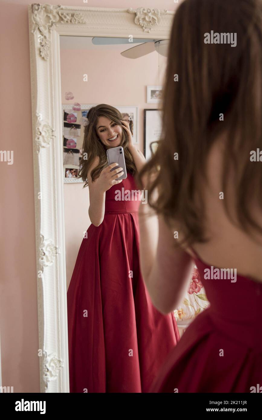 Smiling teenage girl in red prom dress taking selfie at mirror Stock ...
