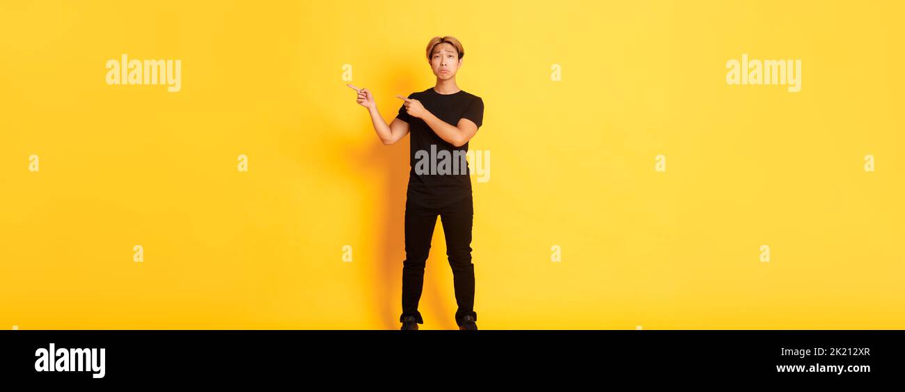 Full-length of sad and miserable asian guy in black clothes, pouting ...