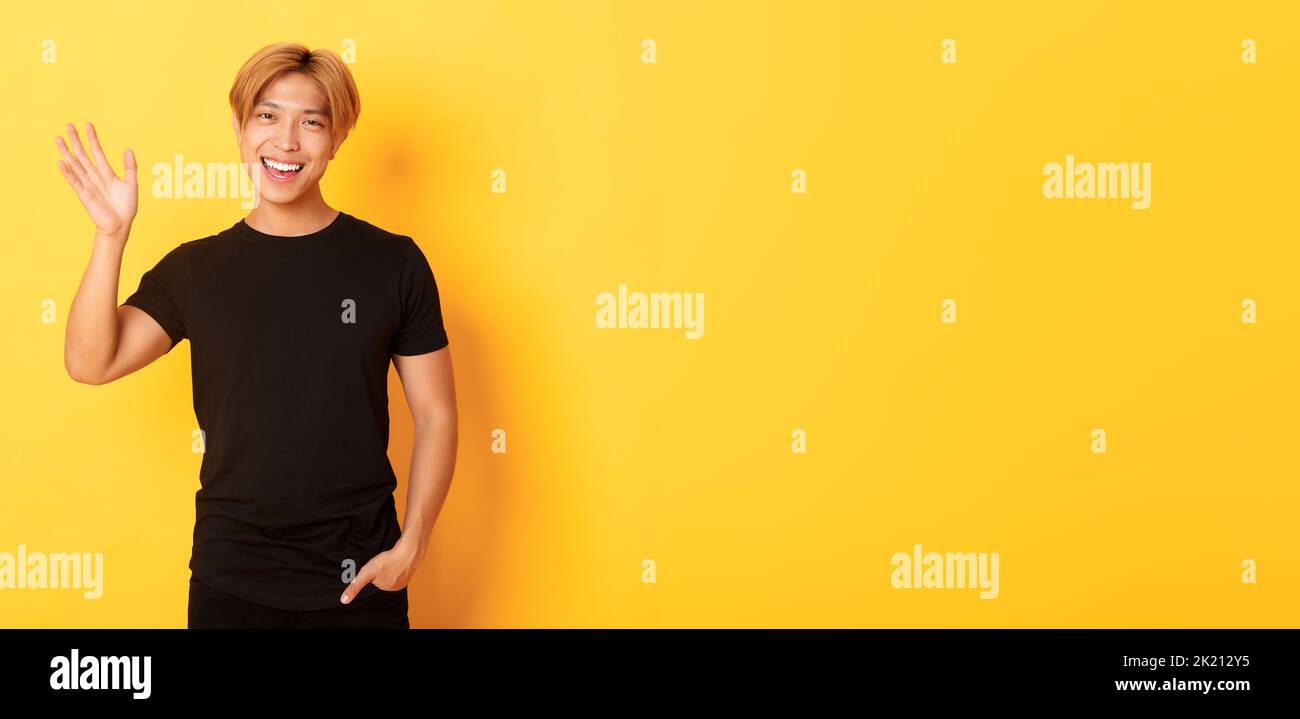 Portrait of handsome friendly asian guy in black outfit, waving hand to ...