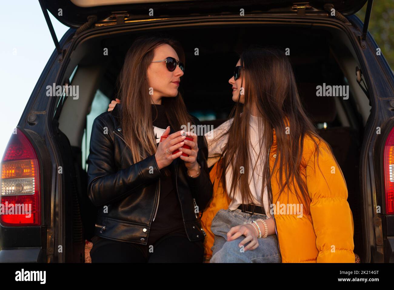 Mother and daughter camping on a hill and admiring the sunset while ...