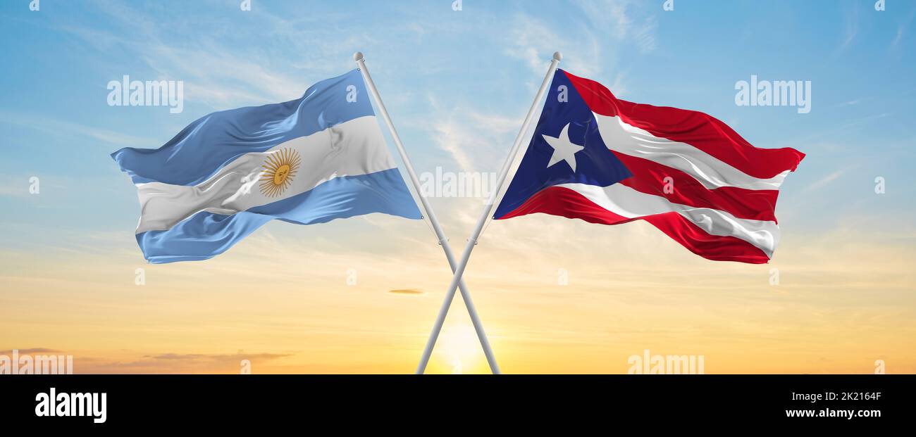 crossed national flags of Argentine and Puerto Rico flag waving in wind at cloudy sky ...