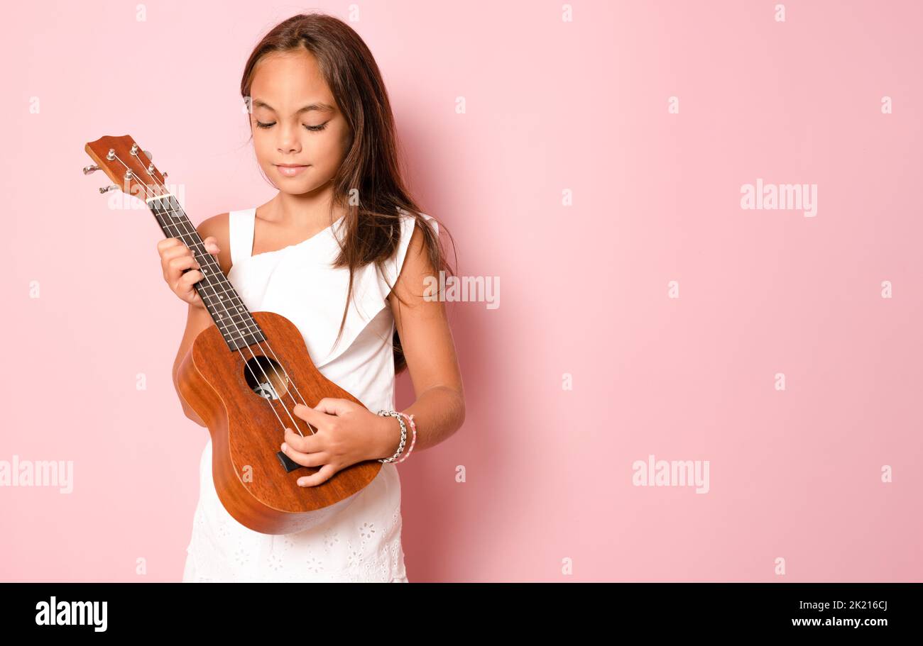 Cute little girl in summer clothing playing ukulele over pink ...