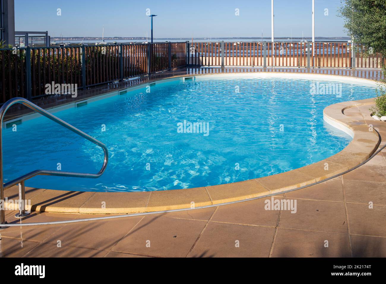 empty oval swimming pool outdoor, morning sunlight, brown fence around ...