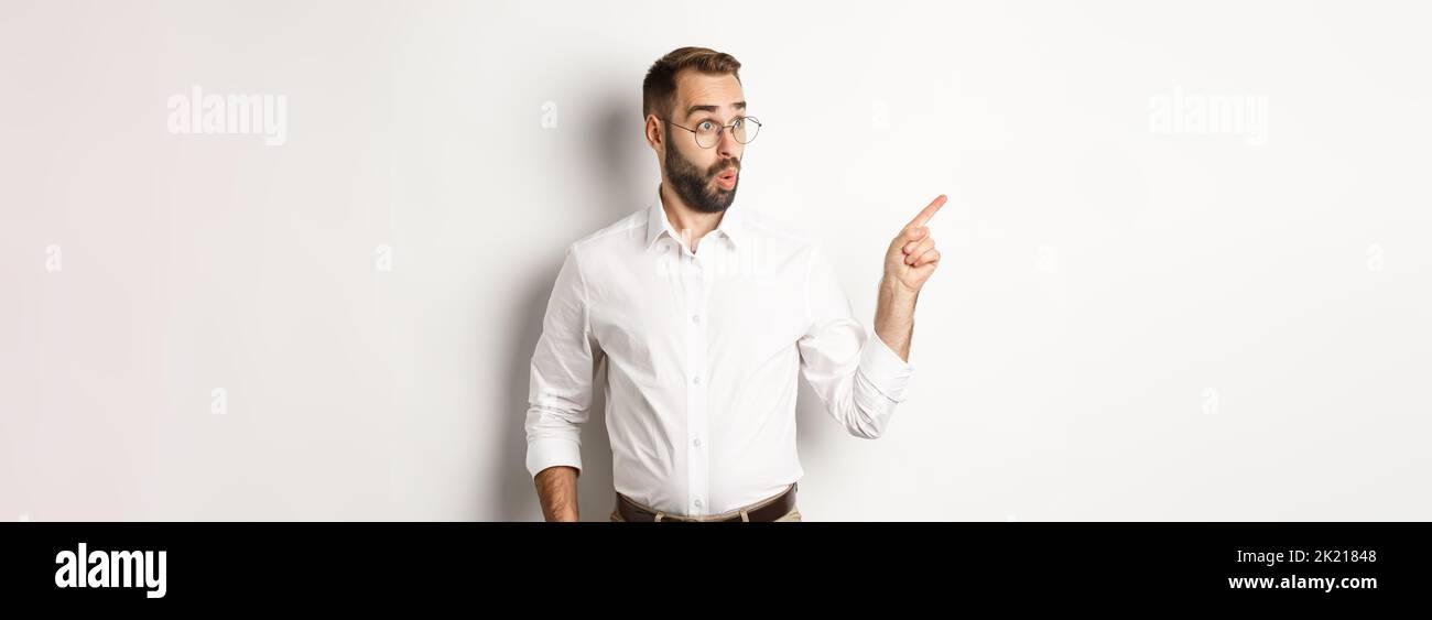 Intrigued young man in glasses pointing finger left, looking at promo ...